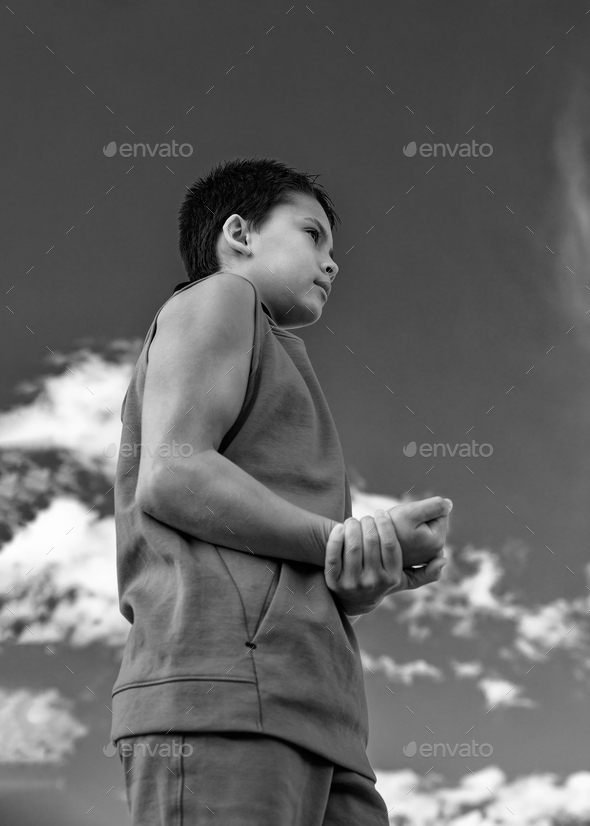 Portrait of teenager boy showing arm muscles against the sky as a ...