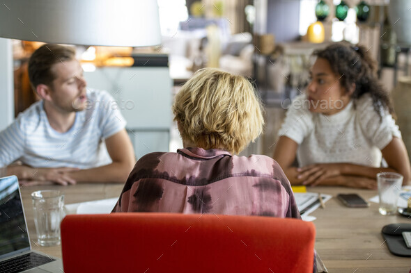 Three young adults engaged in a focused group discussion around a table ...