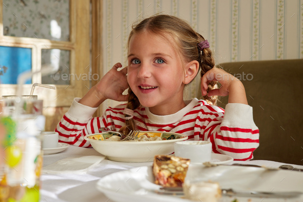 Cute smiling little girl sitting at the dinner table Stock Photo by Demkat