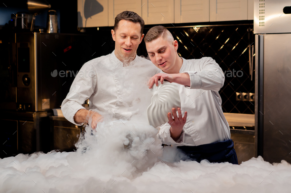 two chefs in white uniforms preparing liquid nitrogen in the kitchen ...