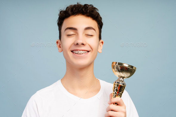 Portrait of smiling boy with braces, winner holding trophy cup, closed ...