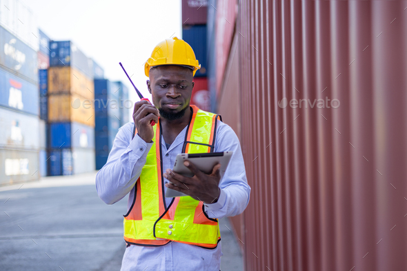 Black engineer in warehouse inspecting goods at industrial container ...