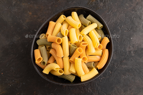 Rigatoni colored raw pasta with tomato, eggs, spices, herbs on black ...