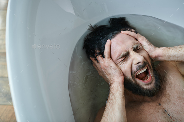 emotional traumatized man lying in bathtub and screaming during ...