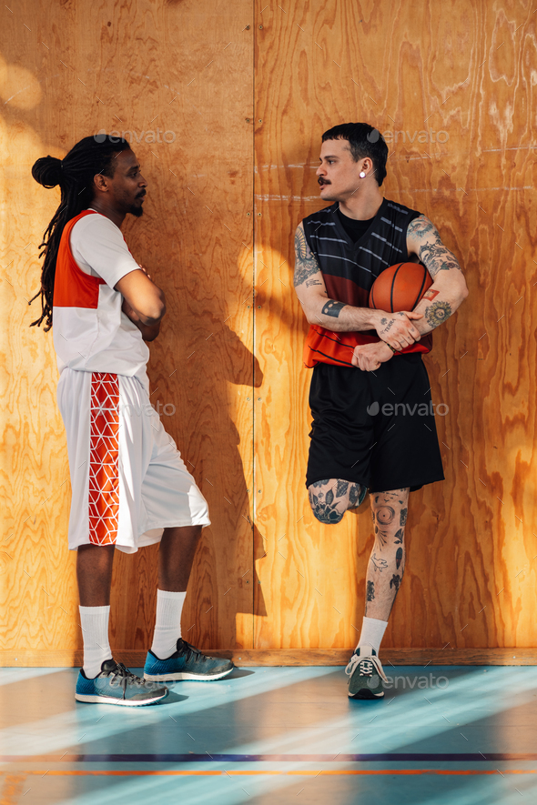 Multicultural basketball players leaning on the wall and chatting ...