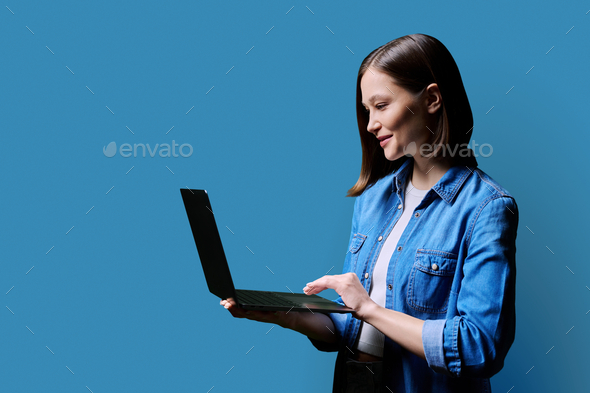 Young smiling woman using laptop, profile view on blue background Stock ...