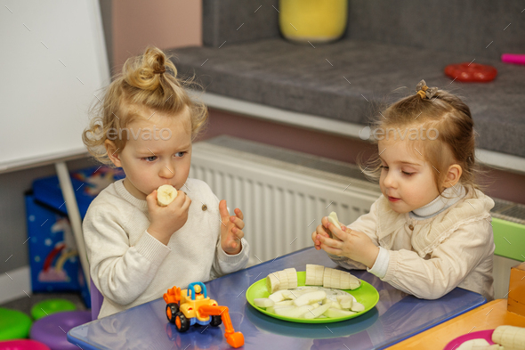 Toddlers Sharing Snack Time at Play Table Stock Photo by OlhaRomaniuk