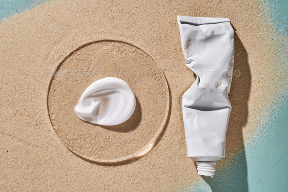 A tube of moisturizing sunscreen and a smear on a sandy background ...
