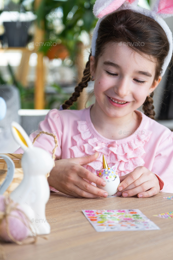 A cute girl with pink bunny ears makes an Easter craft - decorates an ...
