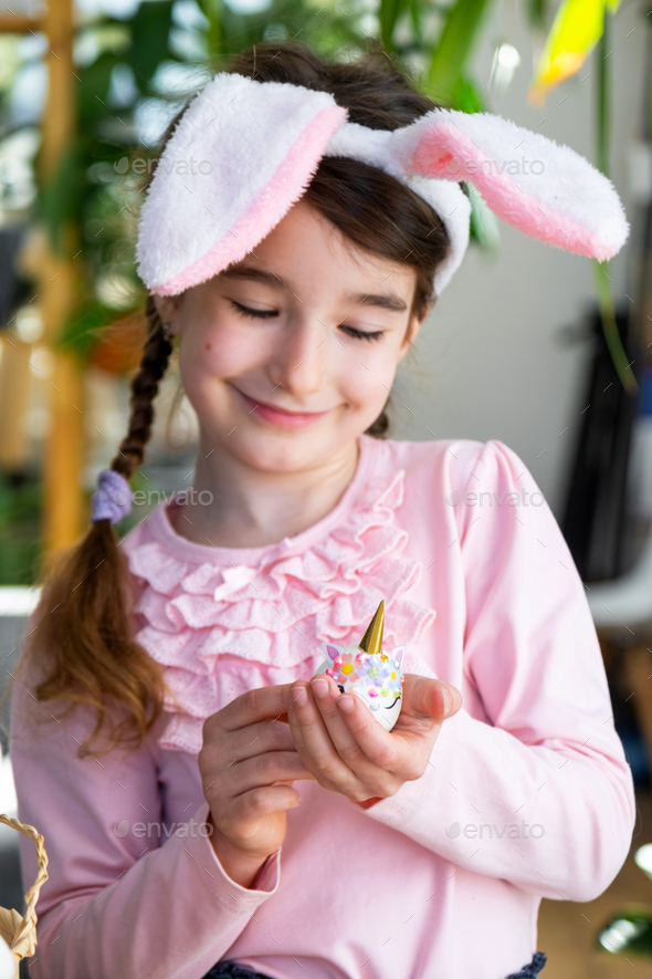 A cute girl with pink bunny ears makes an Easter craft - decorates an ...