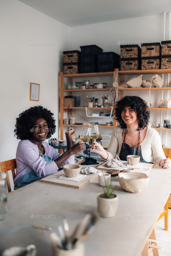 Interracial pottery class students toasting and drinking wine on course ...