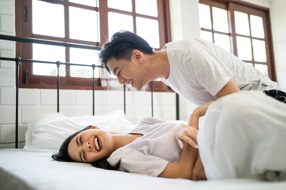 Asian attractive man tickles his girlfriend while lying down on bed ...