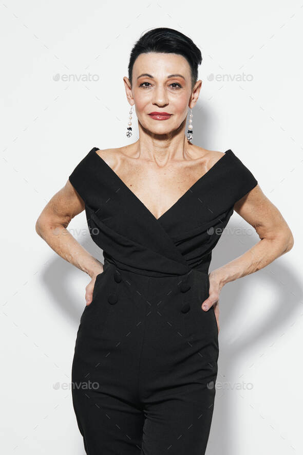 Elegant mature woman in stylish black jumpsuit posing against white ...