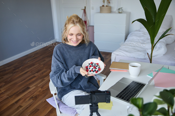 Portrait of cute young girl vlogger, showing her breakfast on camera ...