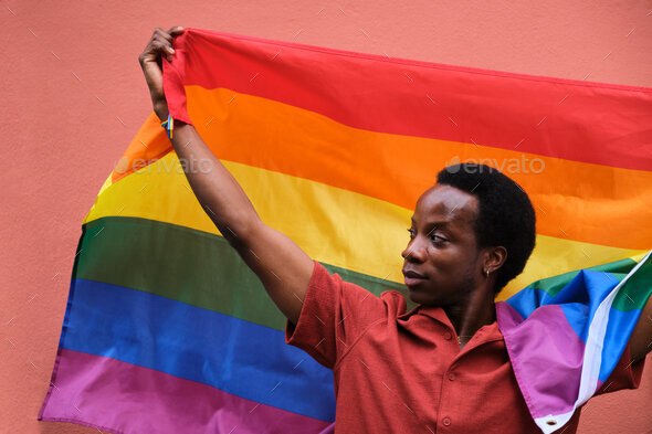 Gay black man holding a rainbow flag representing LGBTQ community ...