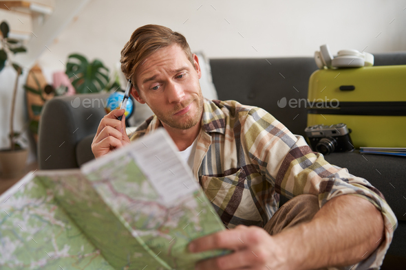Portrait of man, tourist looking confused at travel map, shrugging ...