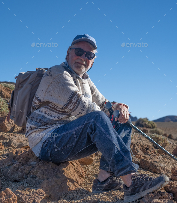 Active elderly man with backpack sitting outdoors in mountain resting ...