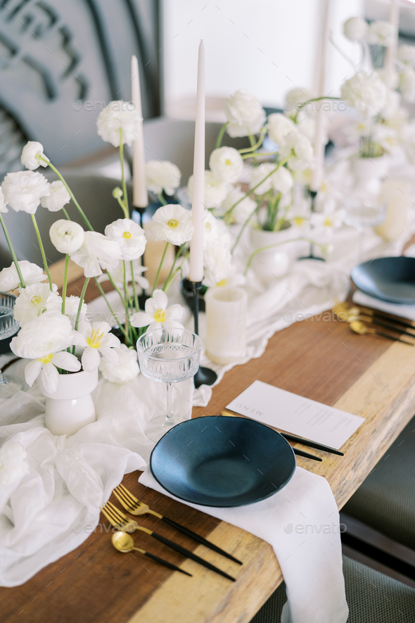 Menus lie near black plates on a festive table with white flowers on a ...