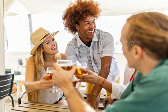 Happy ethnic group of friends cheering with cold beer at beach bar ...