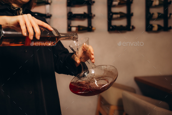 Professional female sommelier pours red wine from decanter to the glass ...