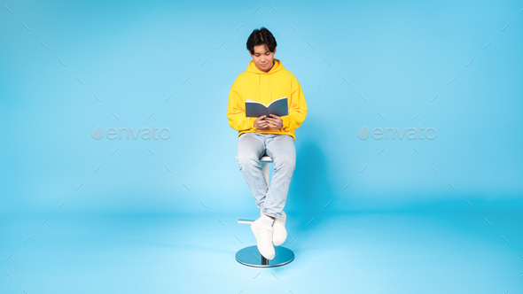 Concentrated teen reading a book on a stool Stock Photo by Prostock-studio
