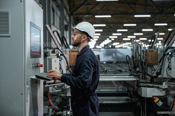 Using equipment, operator. Factory worker is indoors with hard hat ...