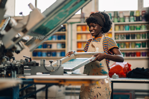 Happy multiracial press woman adjusting screen press for printing ...