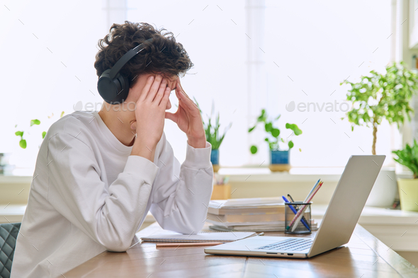 Sad upset young guy in headphones sitting at home at desk with computer ...