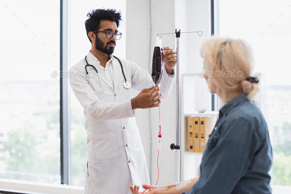 Elderly woman receiving blood transfusion looking at medical doctor ...