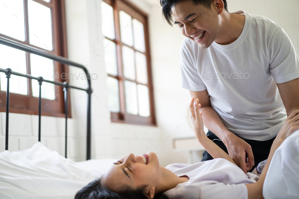 Asian attractive man tickles his girlfriend while lying down on bed ...