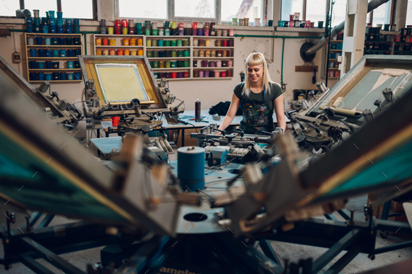 Graphic worker adjusting carousel screen printing machine at print shop ...