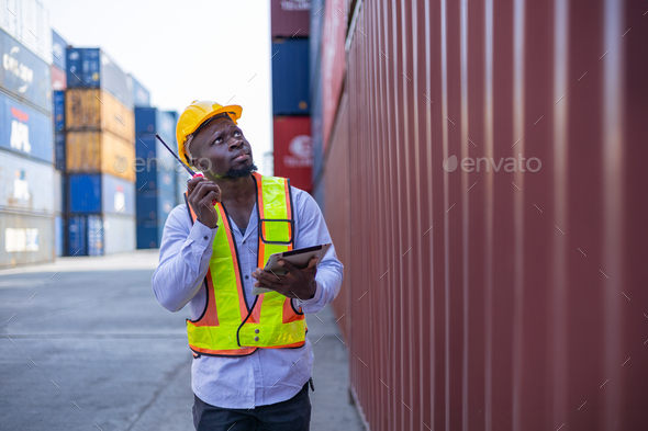 Black engineer in warehouse inspecting goods at industrial container ...