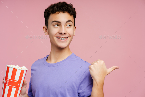 Smiling happy boy teenager with braces holding bucket with popcorn ...