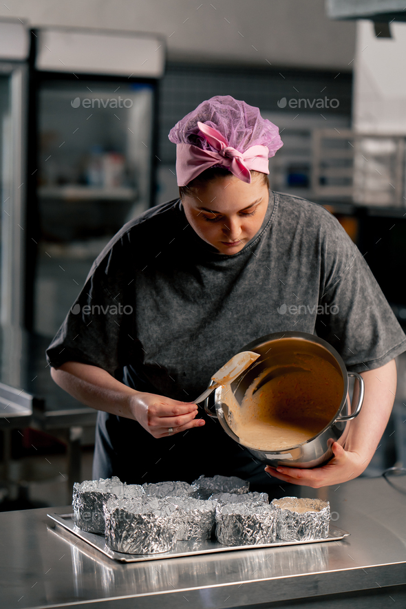 female baker in a professional kitchen pours dough into layers of cake ...