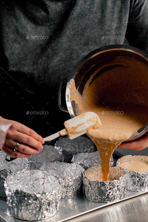 close up hands female baker in a professional kitchen pours dough into ...