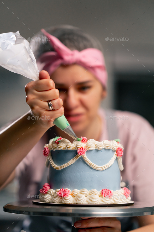 close up of a female baker in a professional kitchen decorating a blue ...