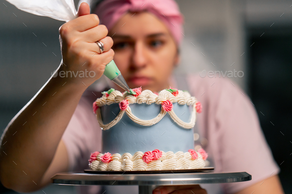 close up of a female baker in a professional kitchen decorating a blue ...