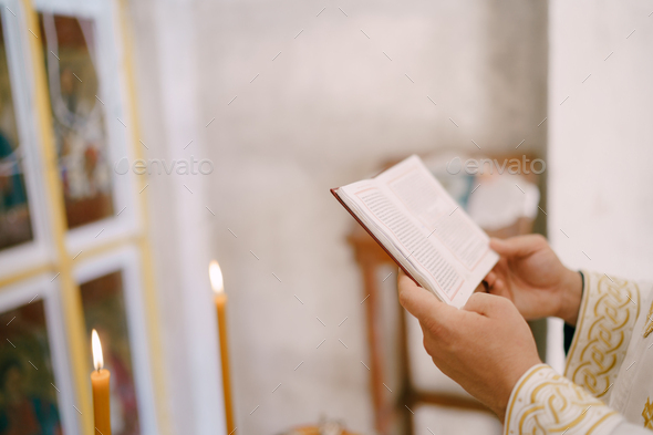 Priest reads the bible near the table with lit candles in the church ...