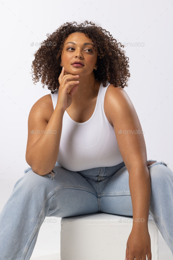 Biracial young female plus size model sitting, touching chin, looking ...