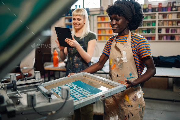Interracial print shop worker putting screen printing plate on a press ...