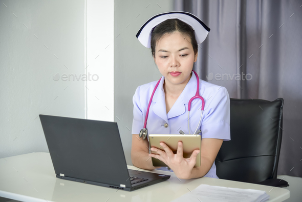 Female Doctor Wearing Scrubs In Hospital Corridor Using Digital Tablet ...