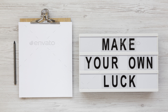 'Make your own luck' on a lightbox, clipboard with blank sheet of paper ...