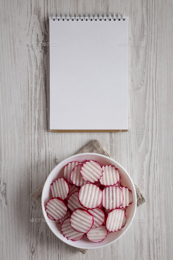Radish Chips Slices in a white bowl, blank notebook on a white wooden ...