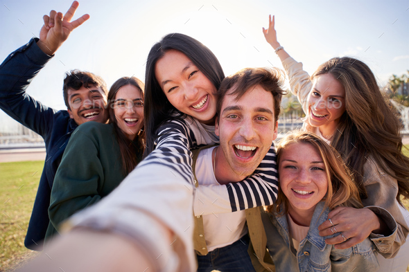 Group diverse happy young friend taking selfie together looking smiling at camera. Piggyback ...