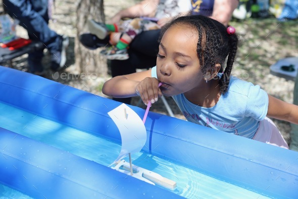 Blow boat racing, a little black girl blowing her sailboat with a straw ...