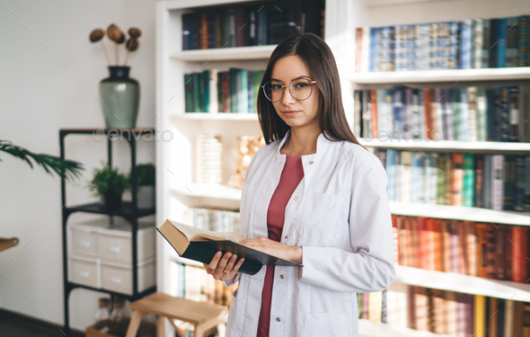 Positive female doctor reading specialized book in library Stock Photo ...
