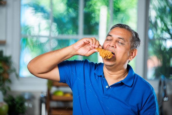 Indian asian mid age handsome man eating chicken leg piece with ...
