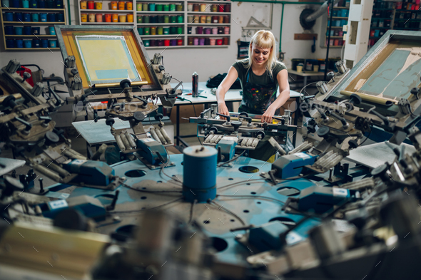 Female graphic worker is screen printing on carousel printing machine ...