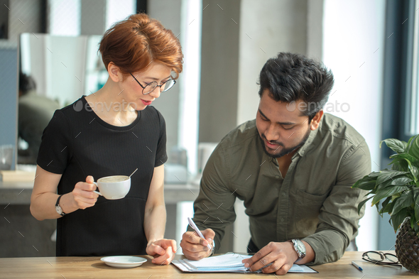 Two business people discuss meeting table with documents and write ...