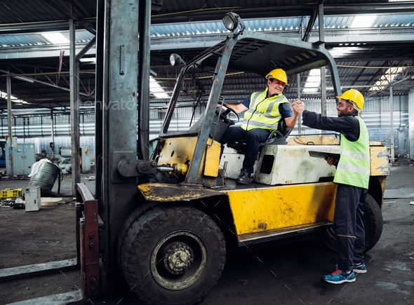Two men are standing next to a forklift, one of them is wearing a ...
